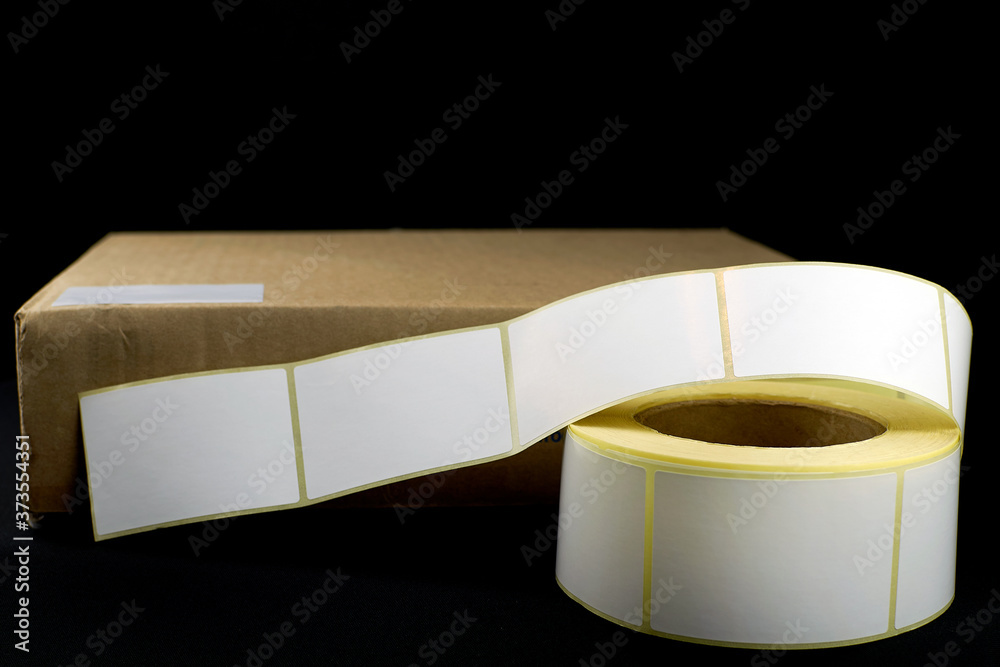 Roller of self-adhesive white stickers on a cardboard box. Cardboard ...