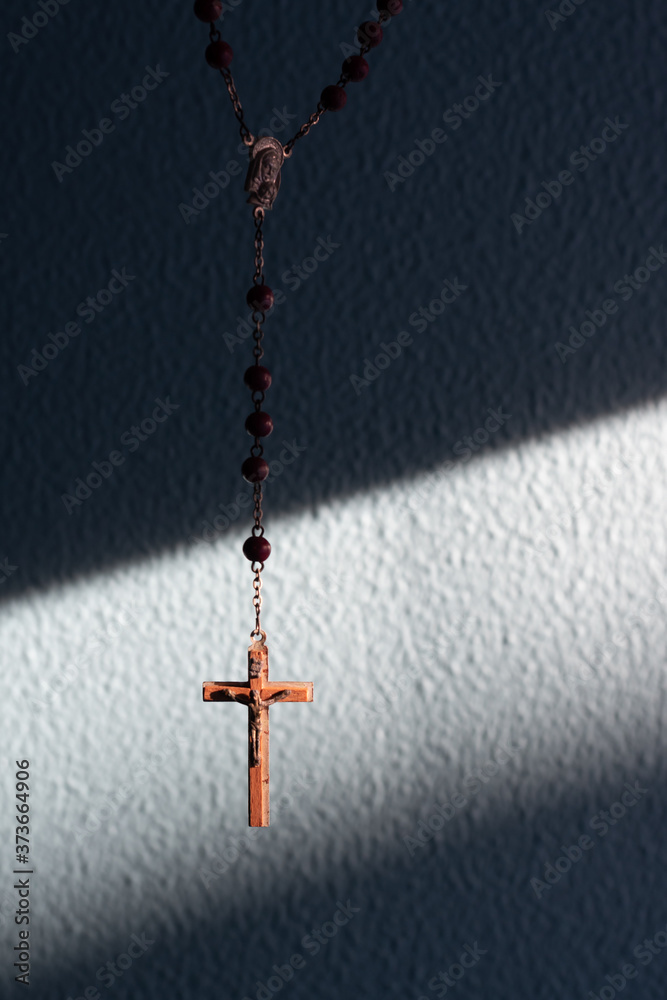 Rosary cross lit by sun hanging over a background diagonal light on ...