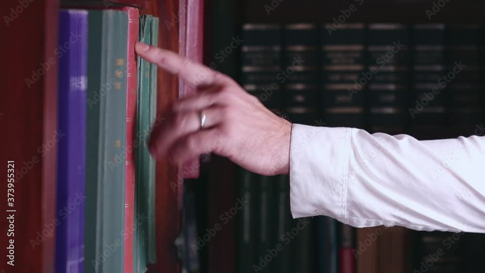 Shallow focus on hand reaching for classic book from library shelf ...