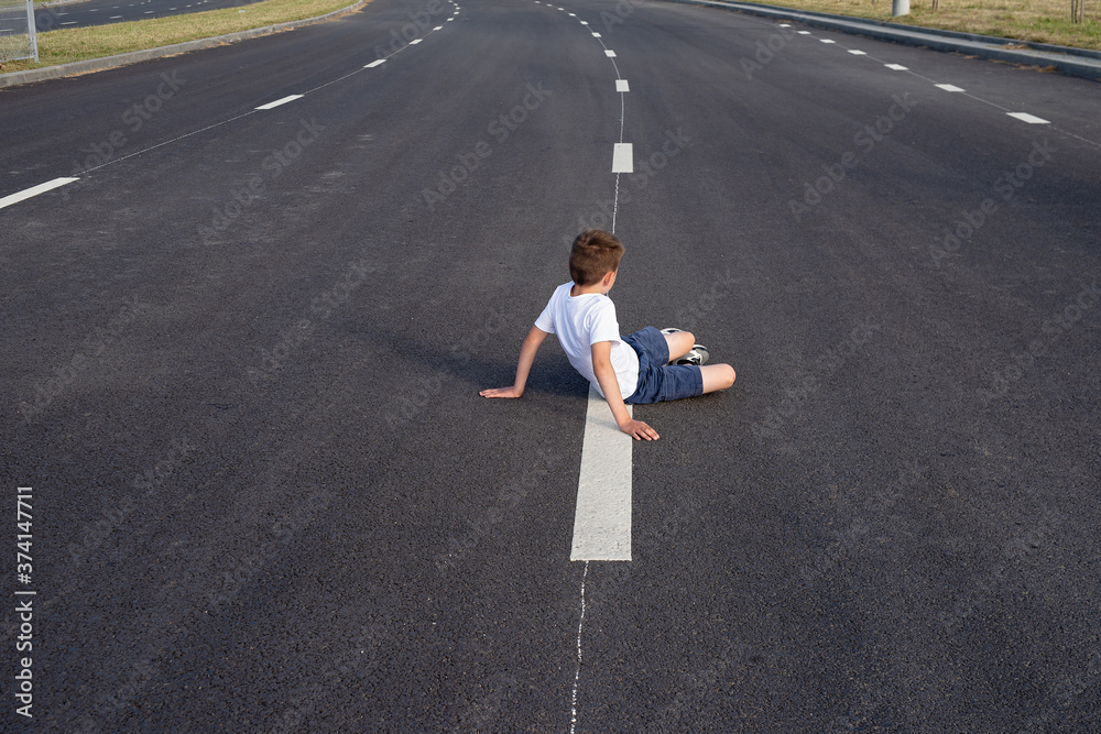 boy sitting on black road with white markings, back view, road safety ...