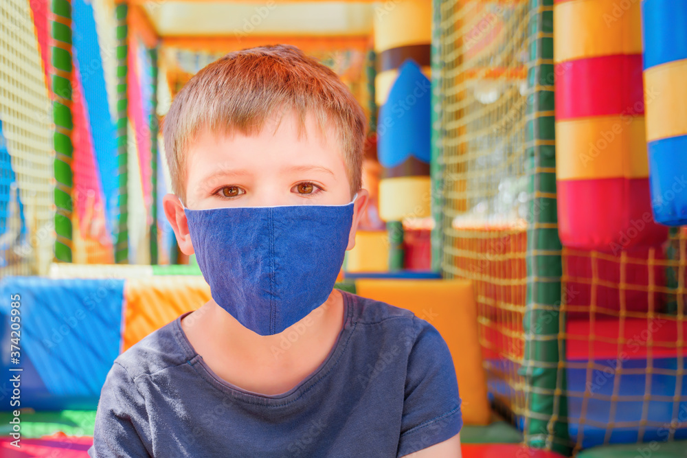 Boy in a medical mask standing near a closed playground. Child in face ...