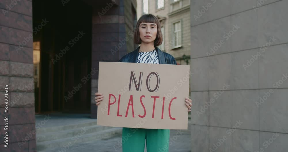 Young serious woman with no plastic poster standing at city street ...
