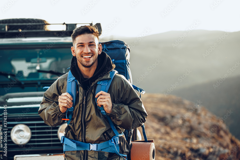 Portrait of a young traveler man in hiking equipment standing near his ...