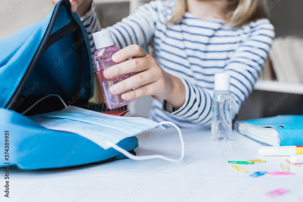 Little girl packing blue backpack in kids's room. Face mask, bottle of ...