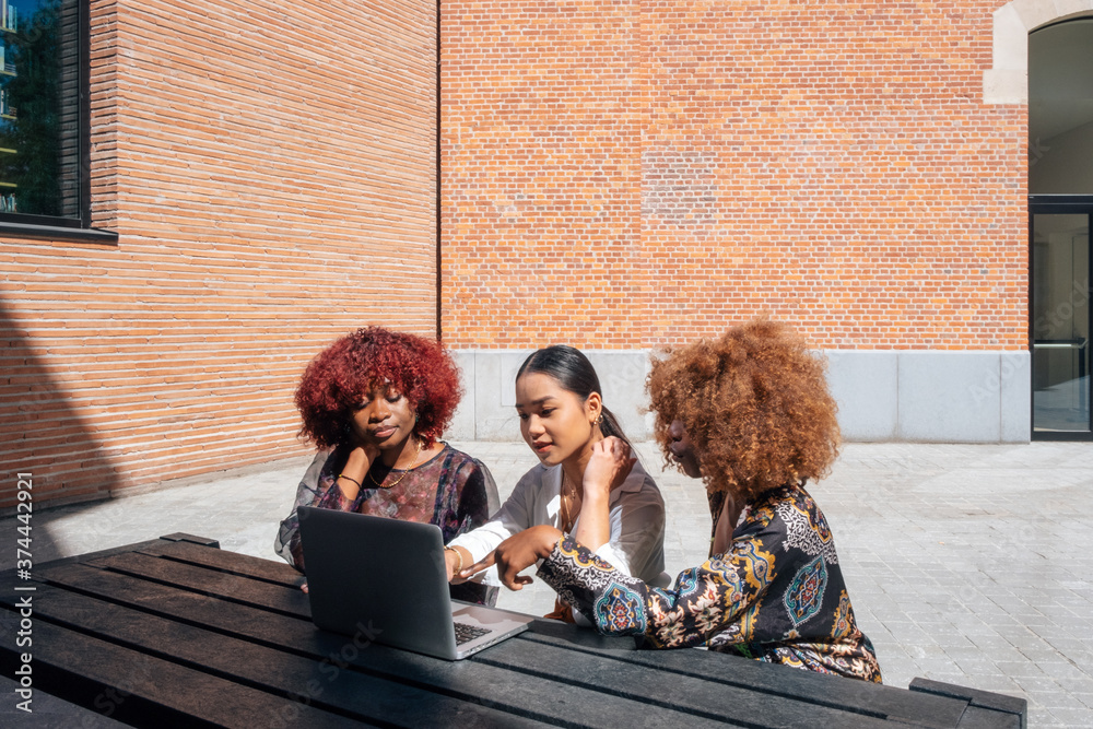multiracial girls students sitting outdoor the university using a ...