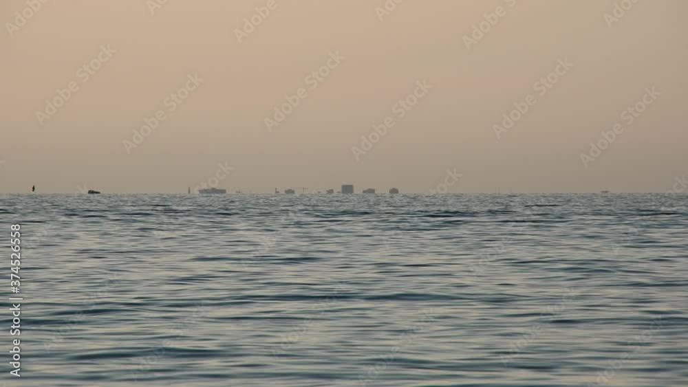 Calm sea waves at sunset. Industry construction behind the horizon ...