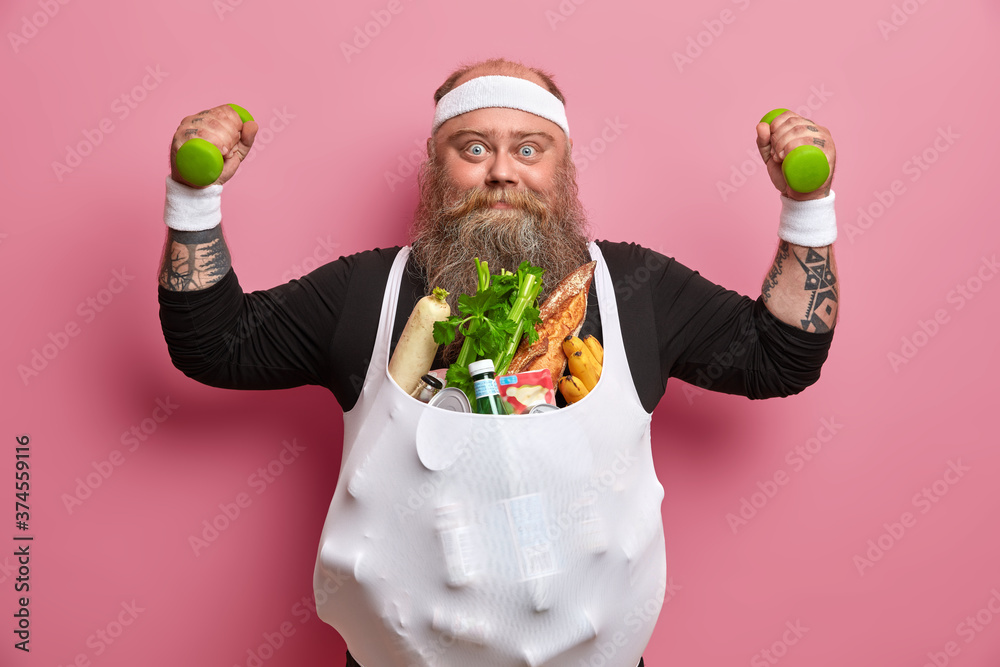Serious overweight man poses with food products, raises dumbbells, does ...