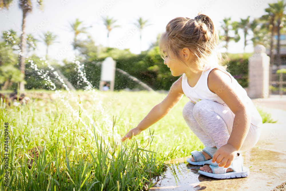 Female blonde cute child bent over the edge of a fountain in the park ...