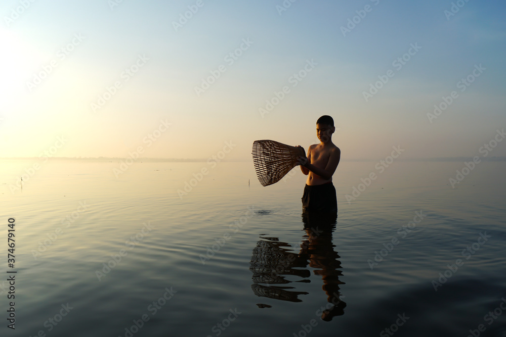 At lake, young asian man using bamboo fish trap to catch fish in the ...