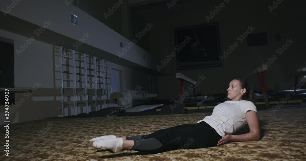 Girl gymnast warms up stretches and kicks twine in sportswear in a dark ...