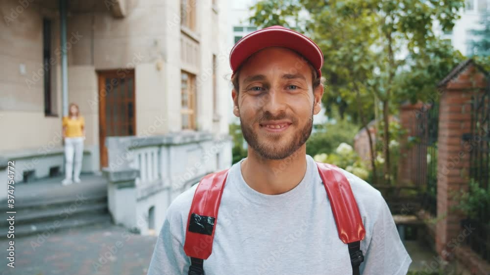 Portrait of joyful bearded mailman in red delivery uniform wearing ...