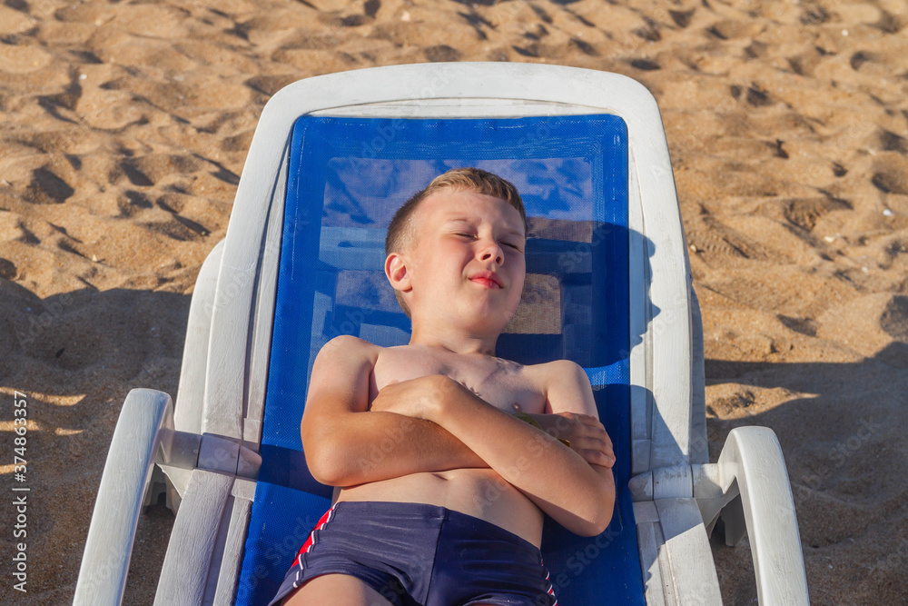 A young European boy with light skin is sunbathing on the beach on a ...