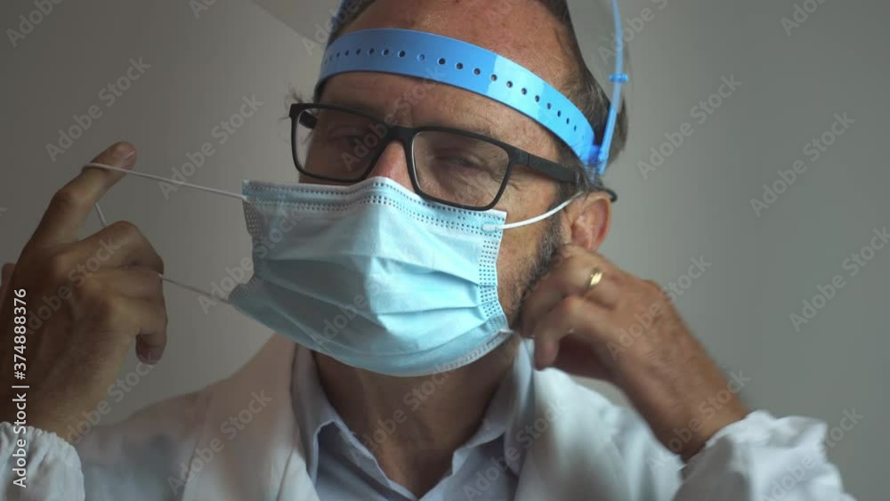 Portrait of a tired handsome male doctor taking off the surgical face ...