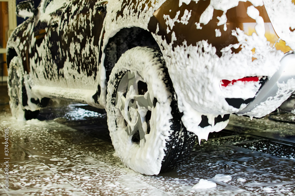 The side part of a brown car, covered in soapy foam at a car wash ...