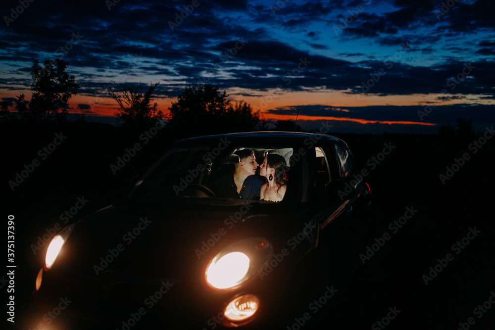 Couple in love sits inside of car with glowing headlights and kisses ...
