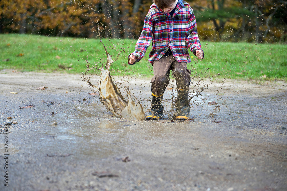 Boy wearing rubber boots splashes in a mud puddle Stock Photo | Adobe Stock