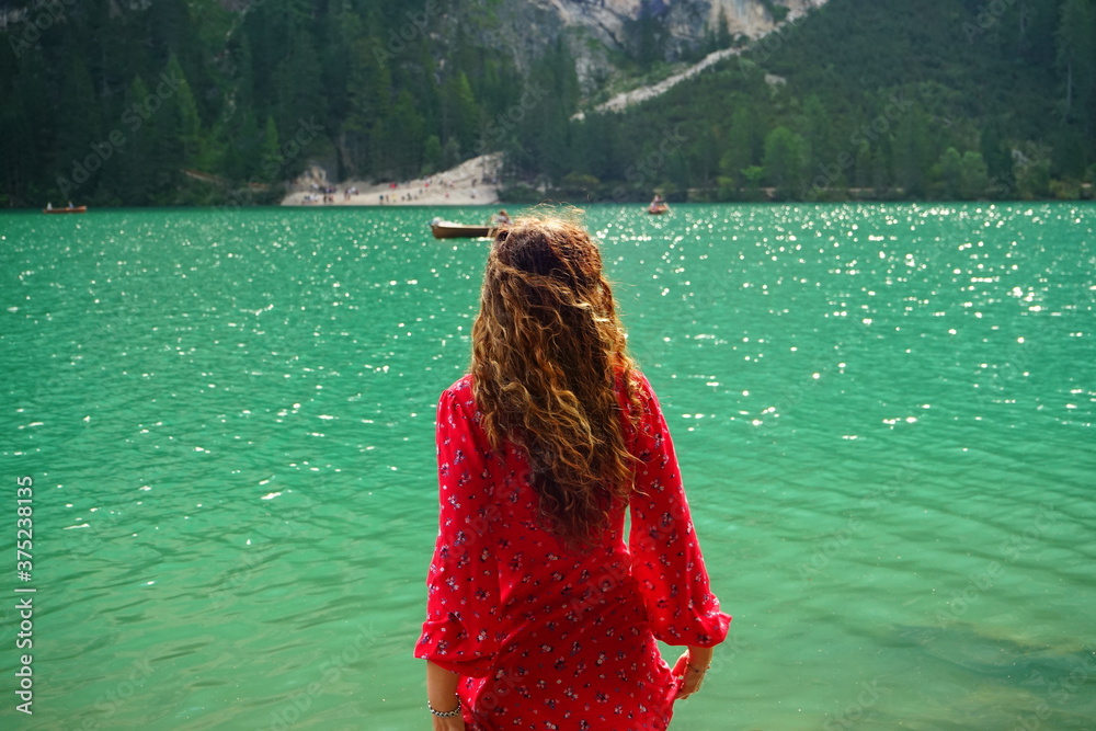 Girl with brown wavy hairs moved by the wind in red dress watching the ...