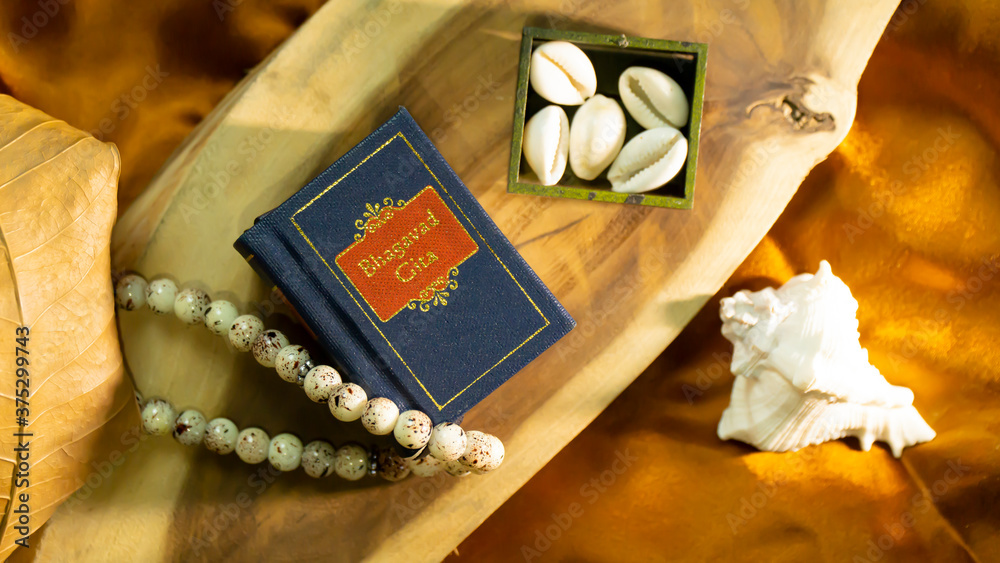Hindu holy book and cowrie shell on a wooden surface with golden satin ...