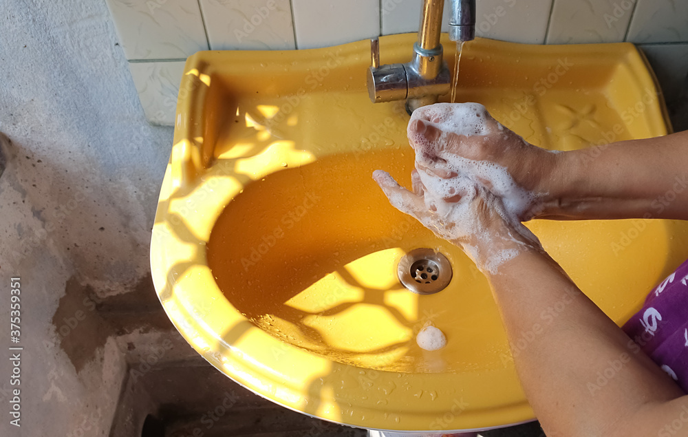 washing of both hands with soap under a yellow wash basin with running ...