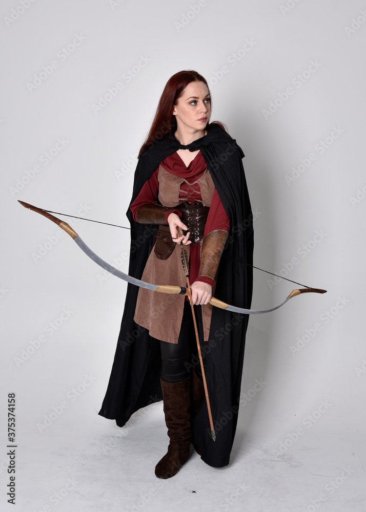 Full length portrait of girl with red hair wearing medieval archer ...