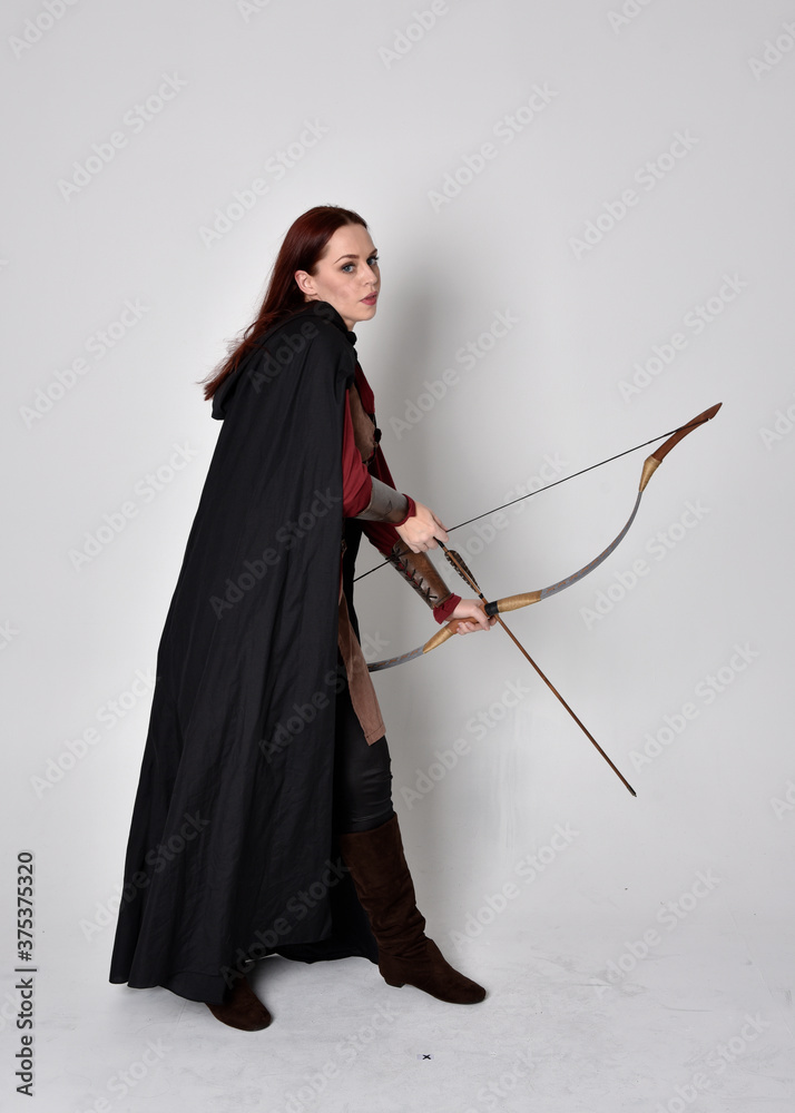 Full length portrait of girl with red hair wearing medieval archer ...