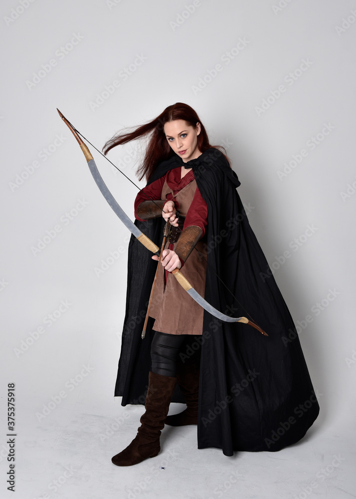 Full length portrait of girl with red hair wearing medieval archer ...