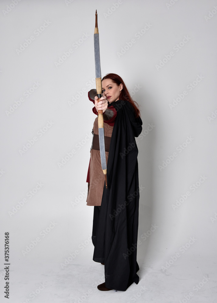 Full length portrait of girl with red hair wearing medieval archer ...