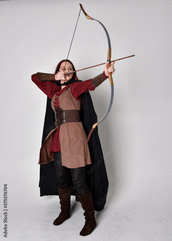 Full length portrait of girl with red hair wearing medieval archer ...