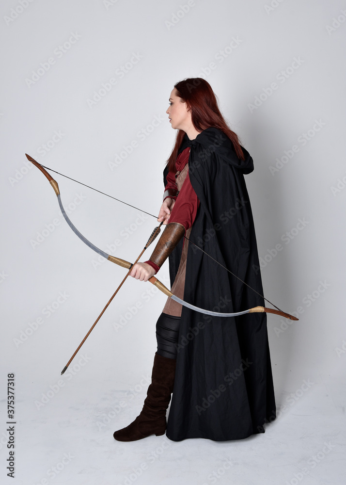 Full length portrait of girl with red hair wearing medieval archer ...