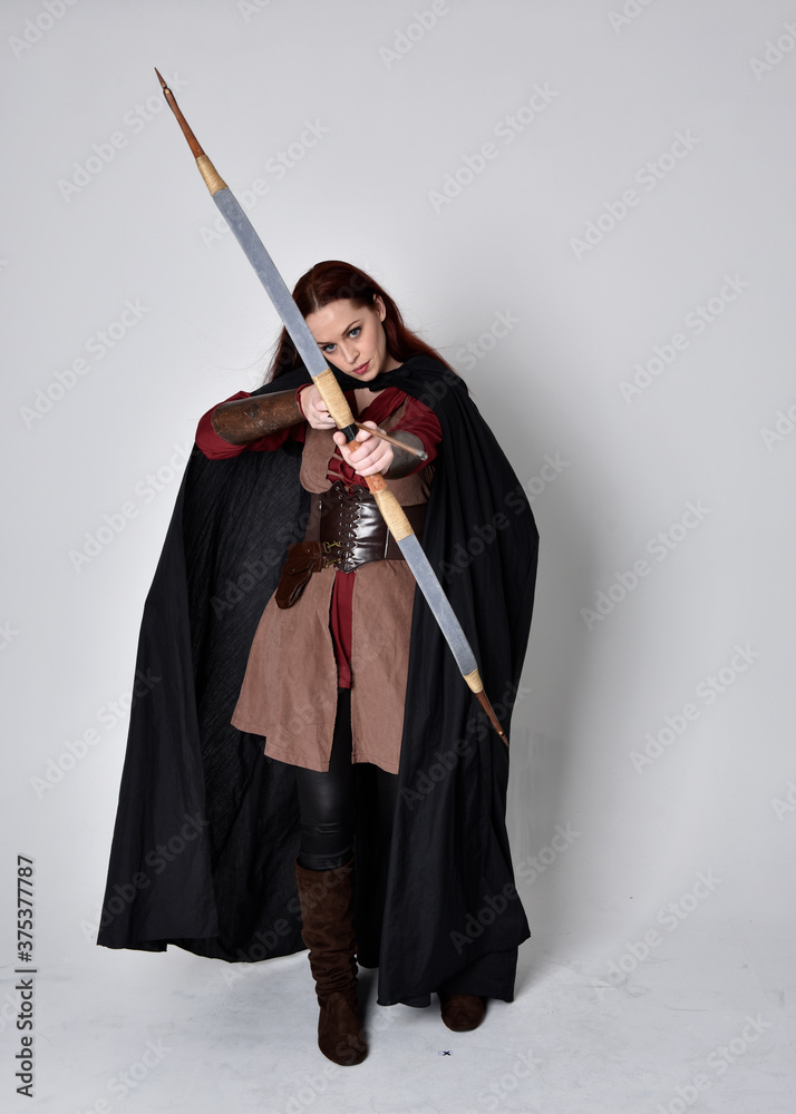 Full length portrait of girl with red hair wearing medieval archer ...