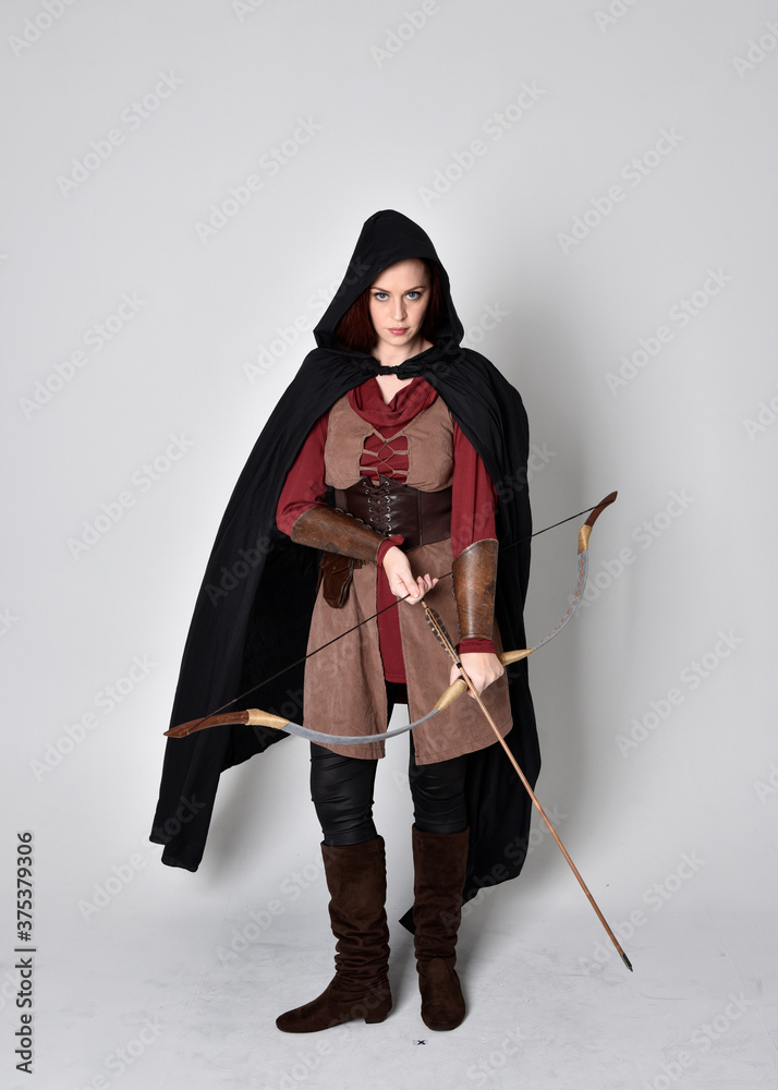 Full length portrait of girl with red hair wearing medieval archer ...