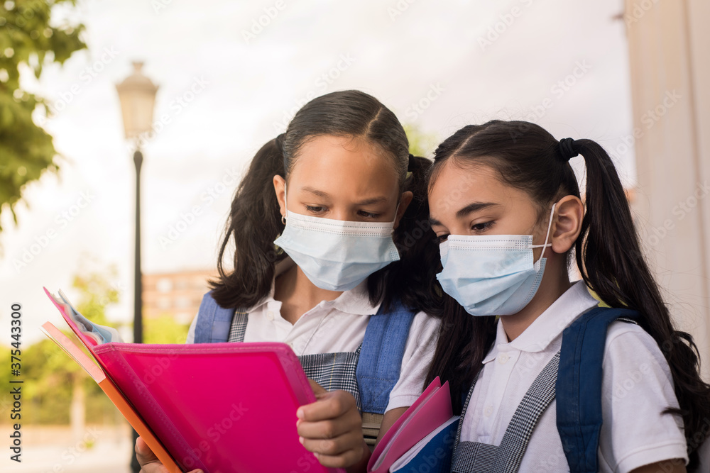 Schoolgirls wear face mask and read the notebook in their hands at ...