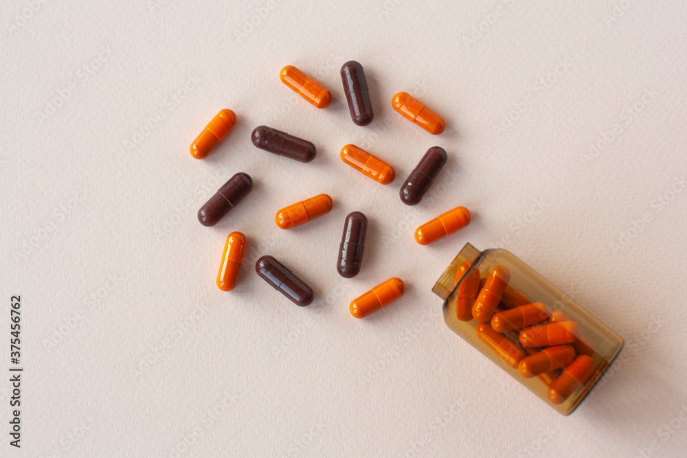 Orange and brown capsules strewn from a glass pill bottle on a peach ...