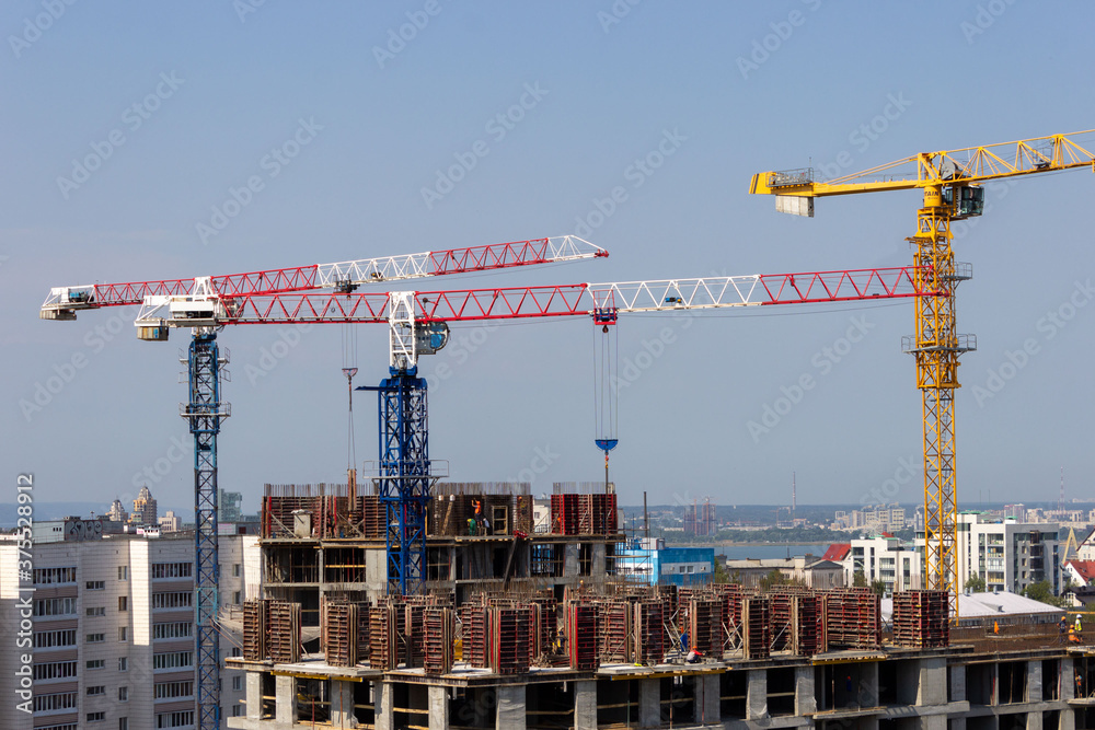 Several high-rise cranes at a construction site, together with people ...