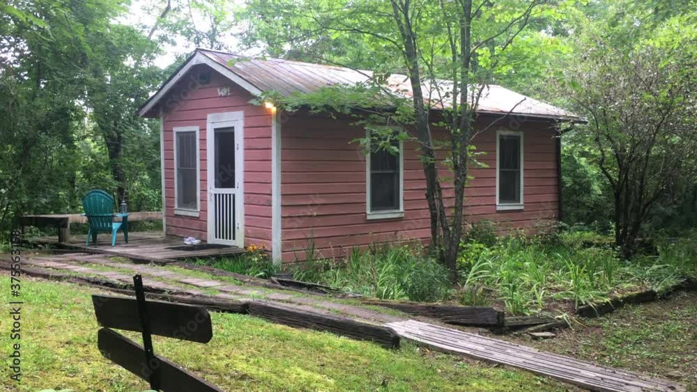 Small pink wooden cabin in the woods with trail signs in front, porch ...