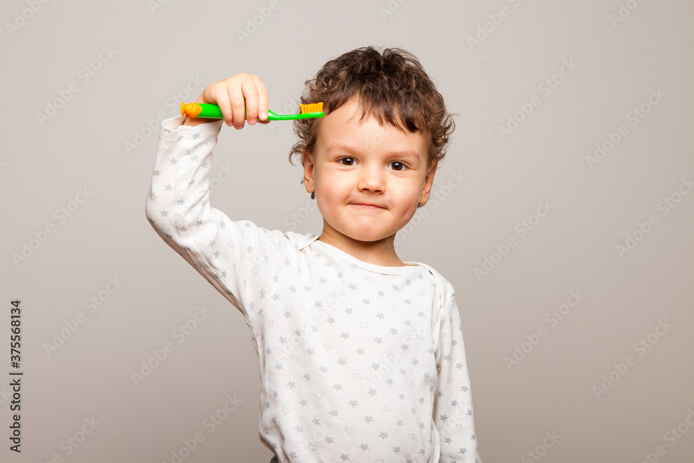 funny curly kid stands smiling and holds a toothbrush in his hands ...