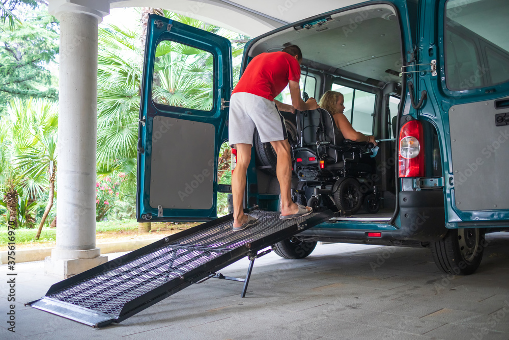 Driver assisting disabled person on wheelchair with transport using ...