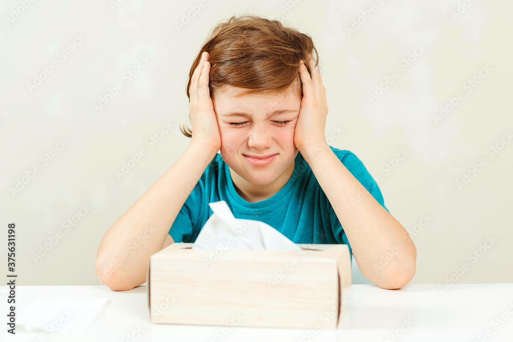 Schoolboy has headache during lessons. Sick boy sitting at the desk ...