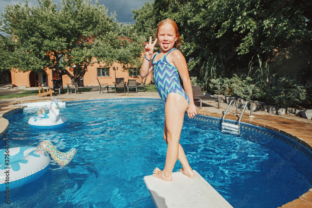 Cute red-haired girl diving in pool from springboard. Child kid ...
