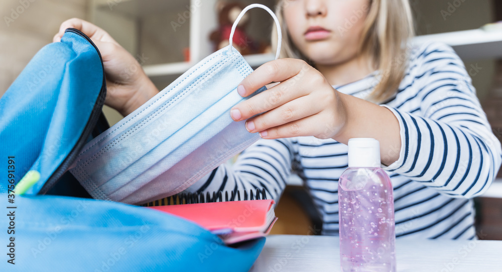 Little girl packing blue backpack in kids's room. Face mask, bottle of ...