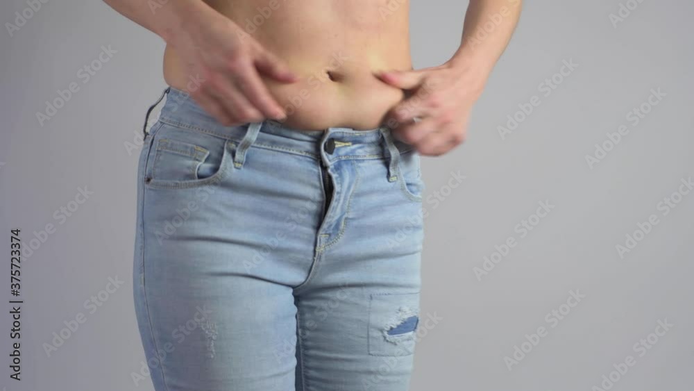 Woman in jeans holds her belly fat. Woman overweight pinch a fat on her ...