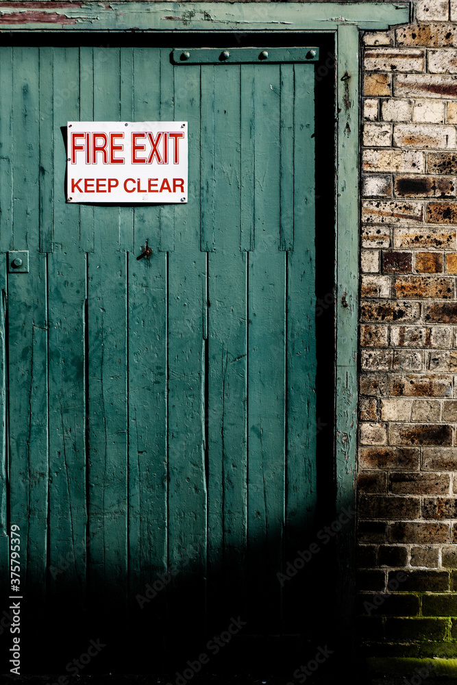 Fire exit sign on an old worn green door against a brick wall. Stock ...