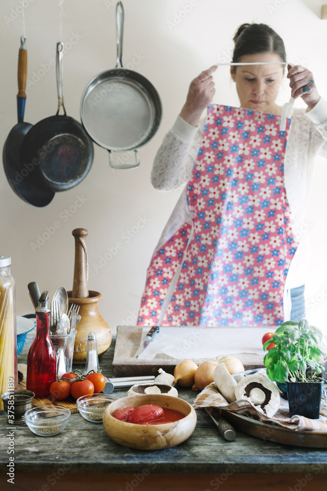 Woman putting on an apron, ready to prepare a meal at her kitchen table ...
