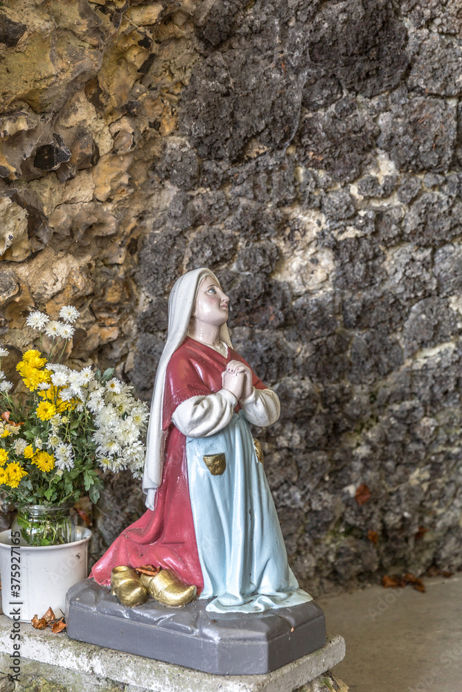 Statue of Bernadette praying to Our Lady of Lourdes with flowers next ...
