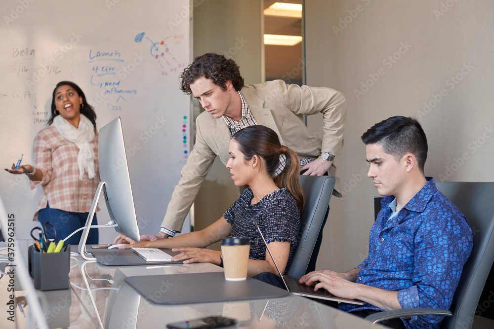 Co-Workers talking at computer in office while woman is working on dry ...