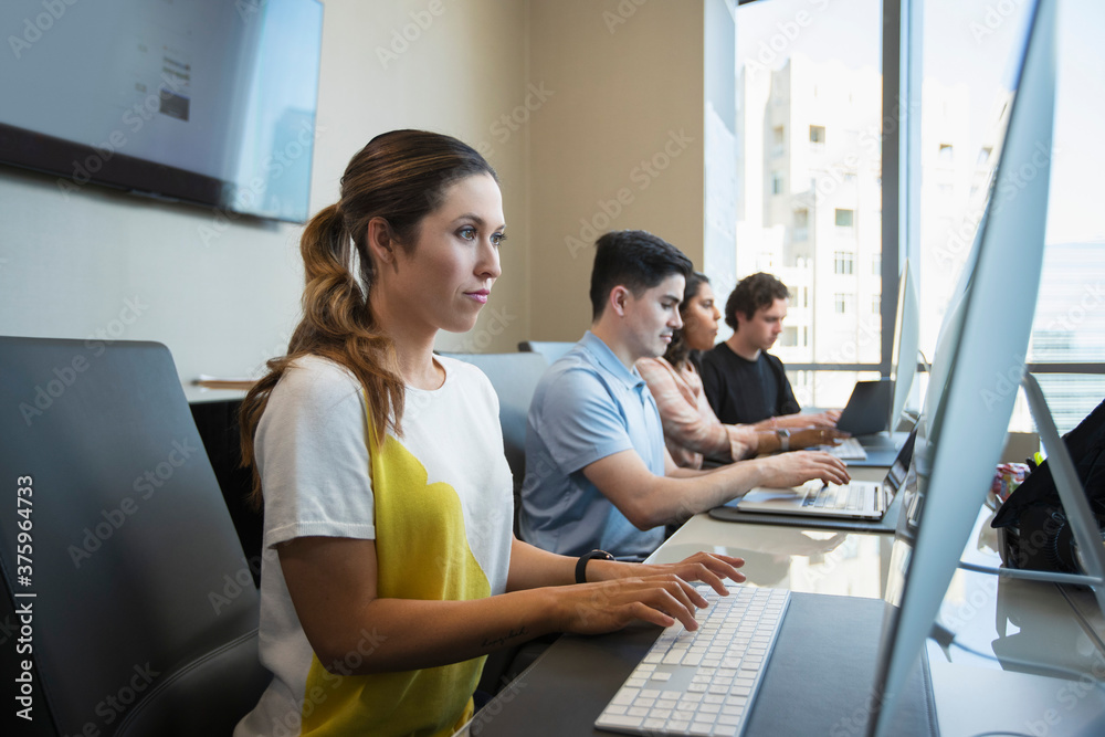 Young woman using computer in office typing on keyboard, co-workers ...