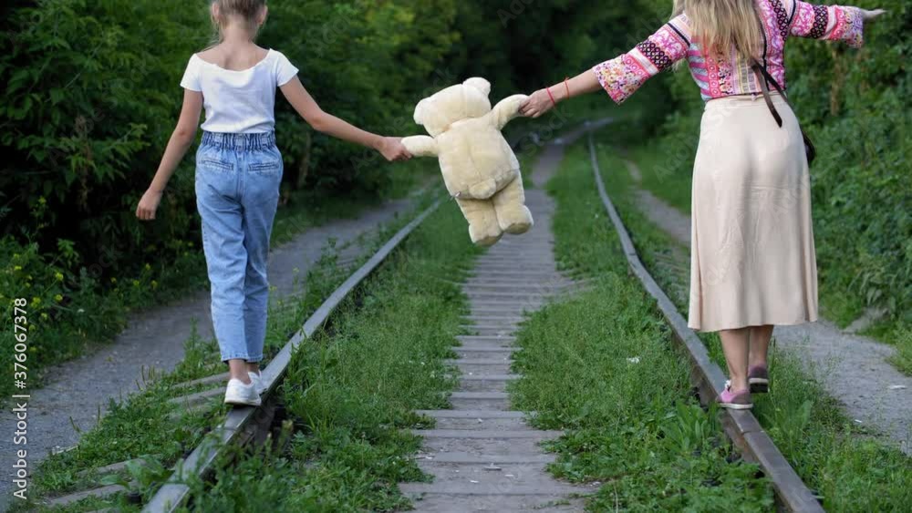 Mom and daughter holding teddy bear walking on train rails at railway ...