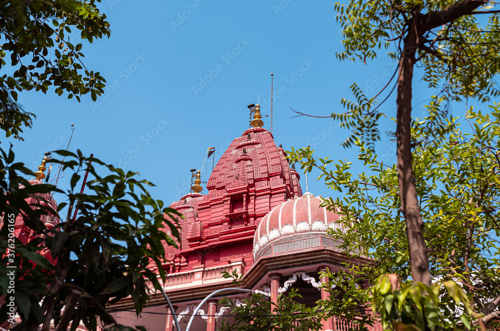 Exterior view of the famous red Digambar jain temple through green tree ...