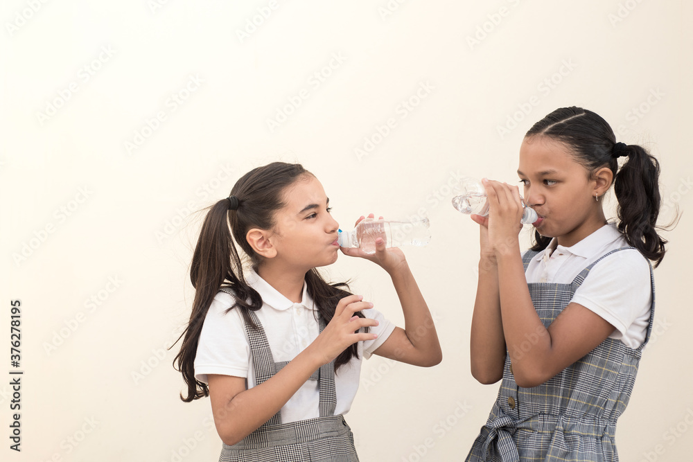 Little classmates looking each other while drink water of bottle ...