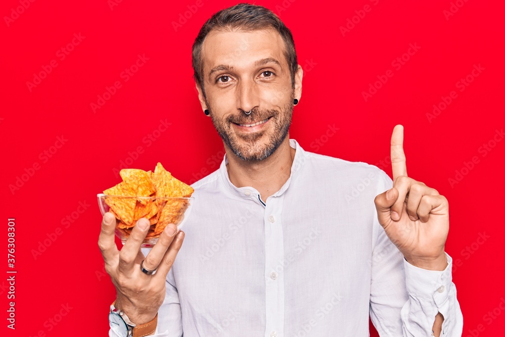 Young handsome man holding nachos potato chips smiling with an idea or ...